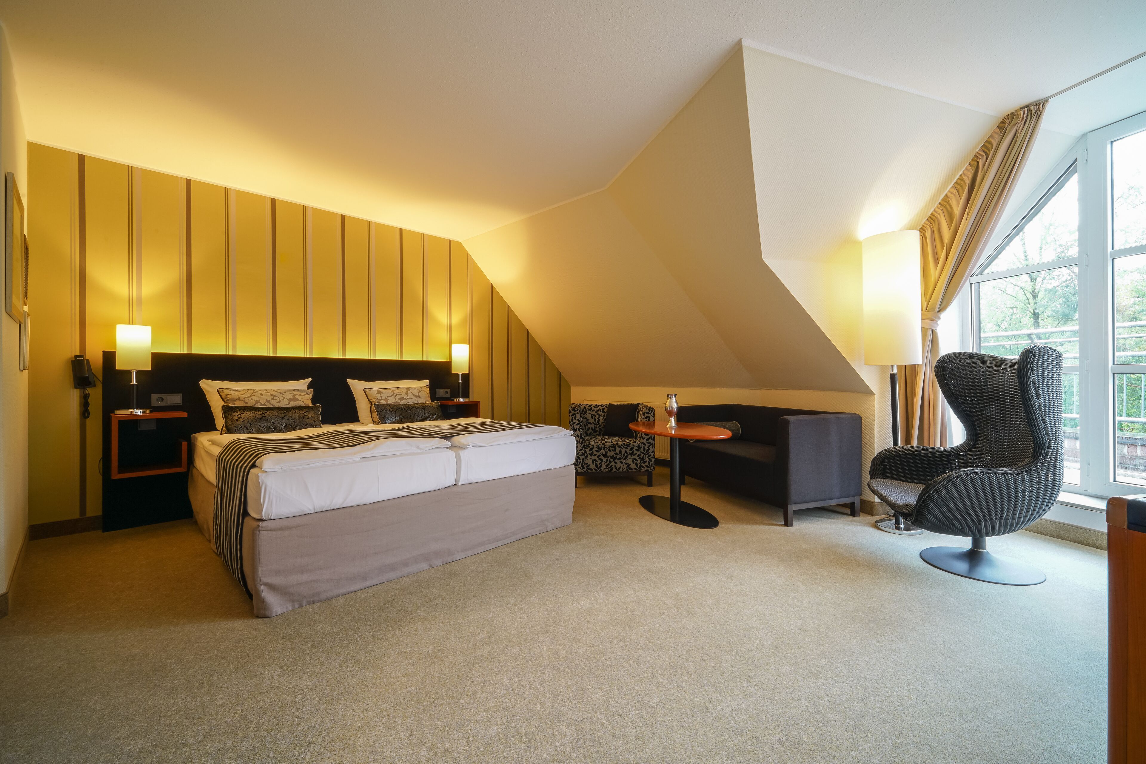 Quarto de hotel moderno com uma cama grande, uma escrivaninha, uma cadeira e uma janela com cortinas.