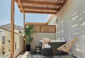 Uma varanda com banheira de hidromassagem, uma cadeira, um vaso de planta e uma pérgola de madeira.