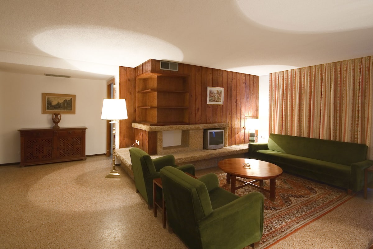 Uma sala de estar com um sofá verde, uma mesa de centro, uma lareira e um armário de madeira.