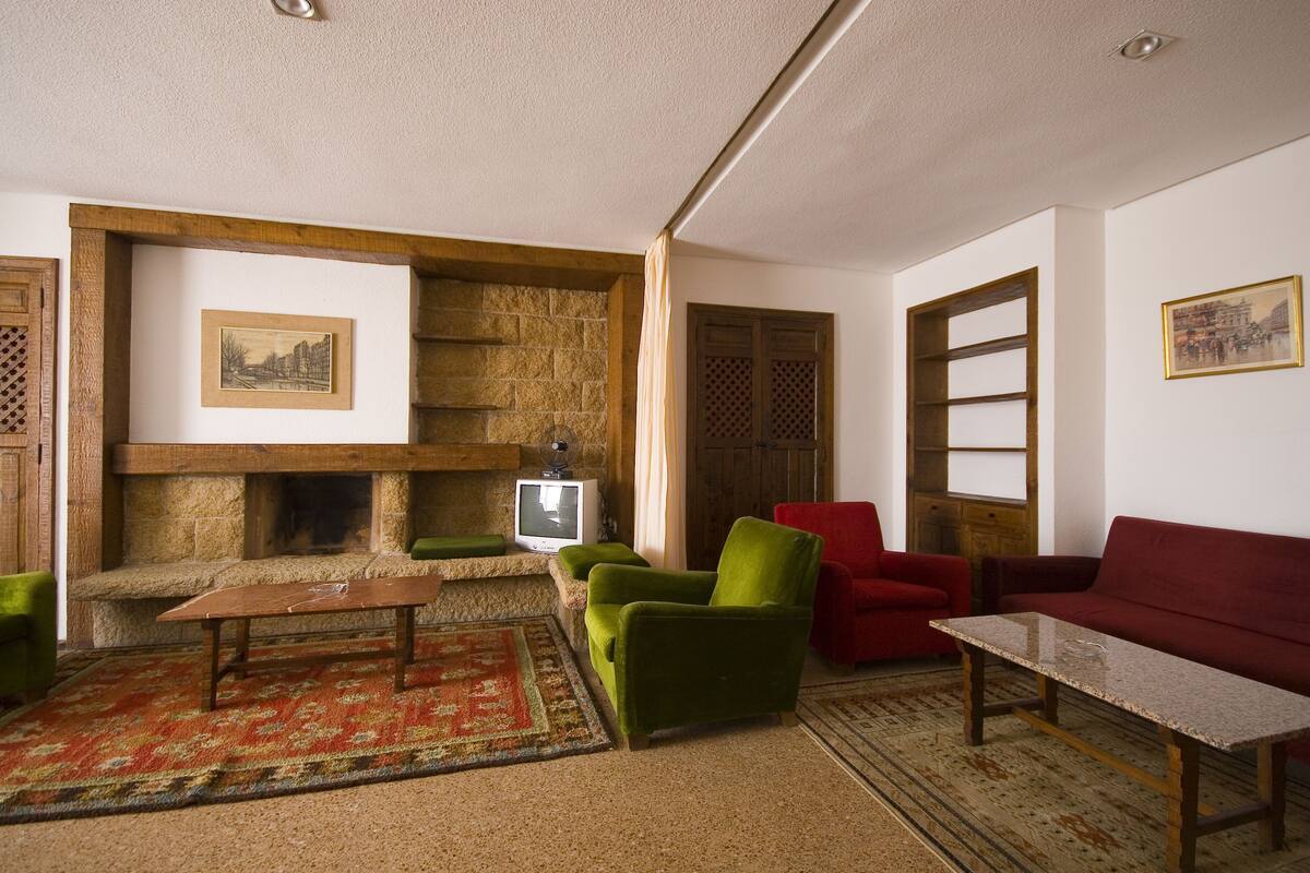 Sala de estar com lareira, sofás verdes e vermelhos, mesa de centro de madeira e uma televisão.
