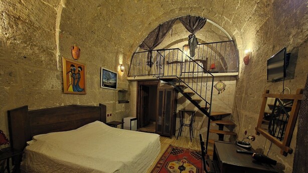 Quarto com cama, escrivaninha, cadeira, televisão e escada para um andar superior.