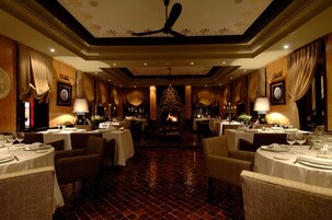 Uma sala de jantar formal com mesas postas, lareira e ventilador de teto.