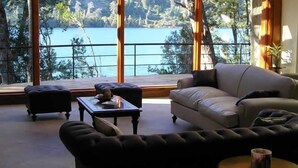 Sala de estar com uma grande janela com vista para um lago, mobiliada com um sofá, duas poltronas e uma mesa de centro.