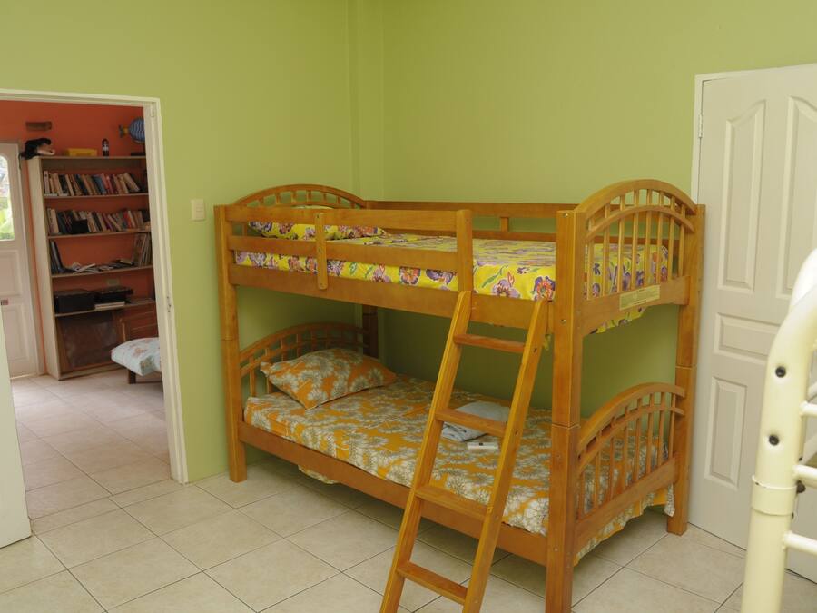 Uma cama beliche com escada, uma estante e uma porta num quarto com paredes verdes e chão ladrilhado.