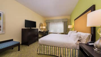 Quarto de hotel com cama, escrivaninha, televisão, abajur e cadeira.