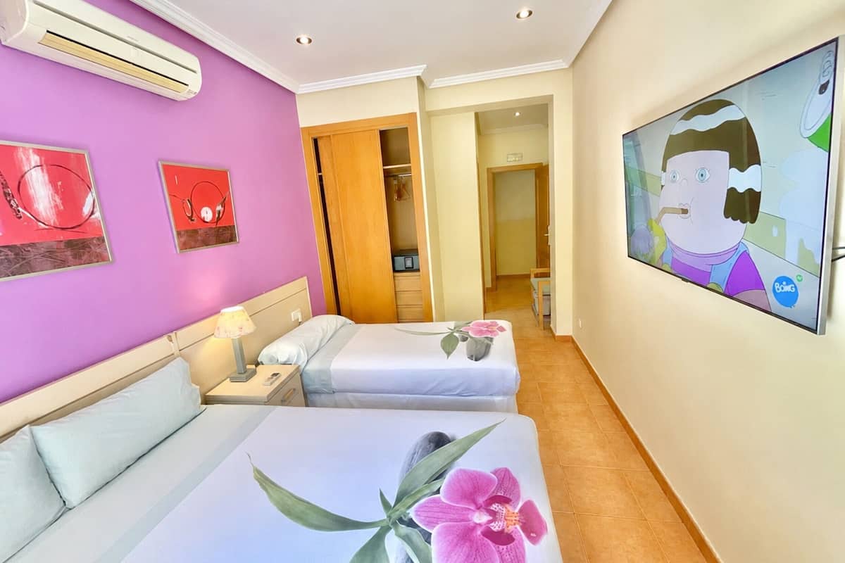 Quarto de hotel com duas camas, televisão, ar condicionado e um quadro na parede.