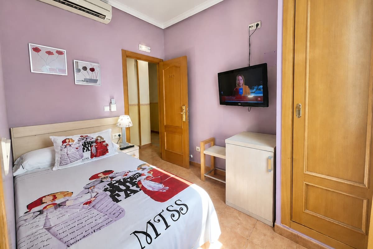 Quarto com cama, televisão, escrivaninha e guarda-roupa.