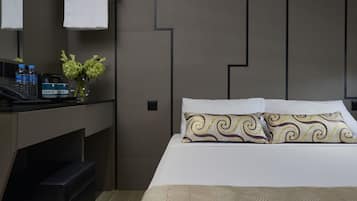 Quarto de hotel com cama, escrivaninha com telefone, um vaso de flores e uma placa indicando o número do quarto.
