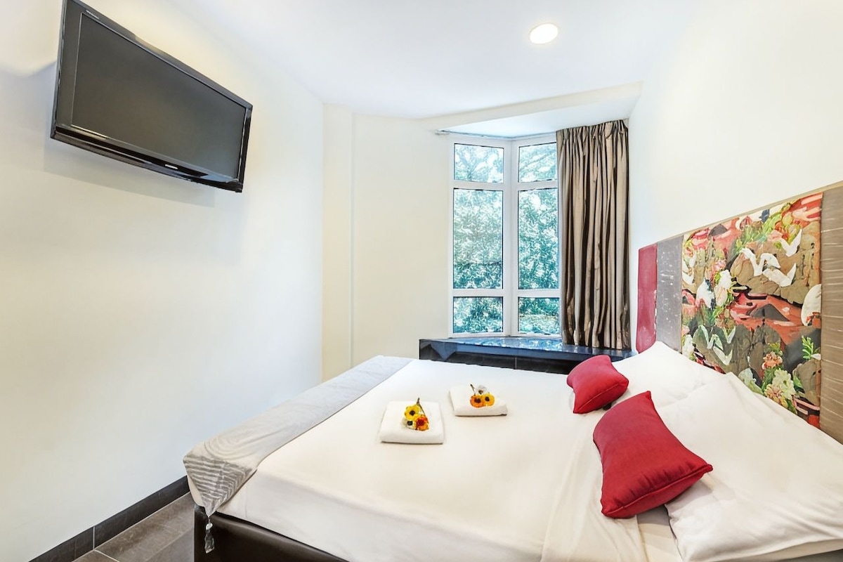 Quarto de hotel com cama, televisão de tela plana na parede, janela com cortinas e cabeceira estampada.