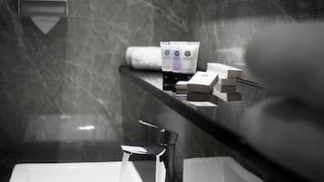 Casa de banho moderna com parede de mármore, lavatório cromado e produtos de higiene num armário.