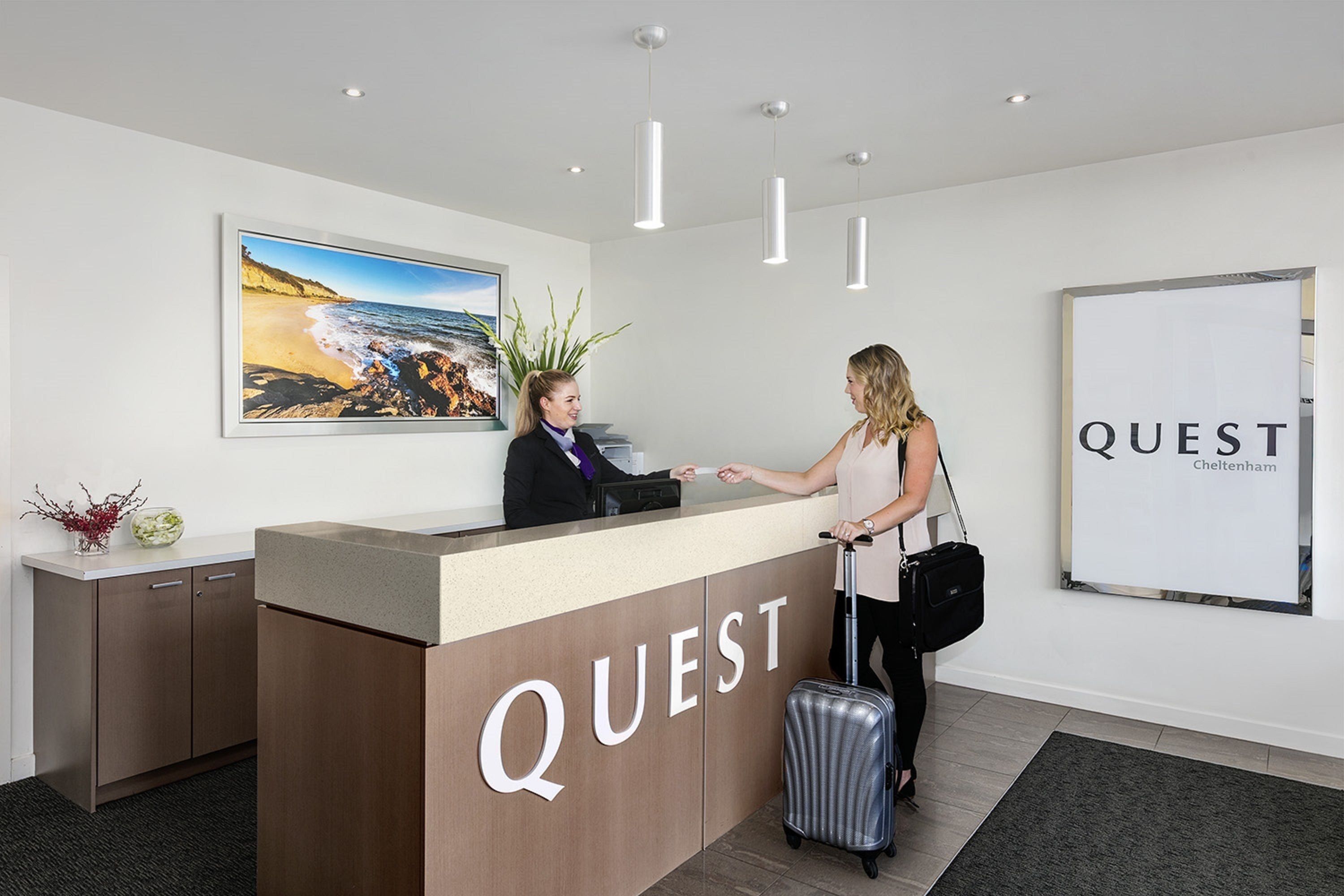 Uma receção com o letreiro "QUEST", um recepcionista e um hóspede com mala.