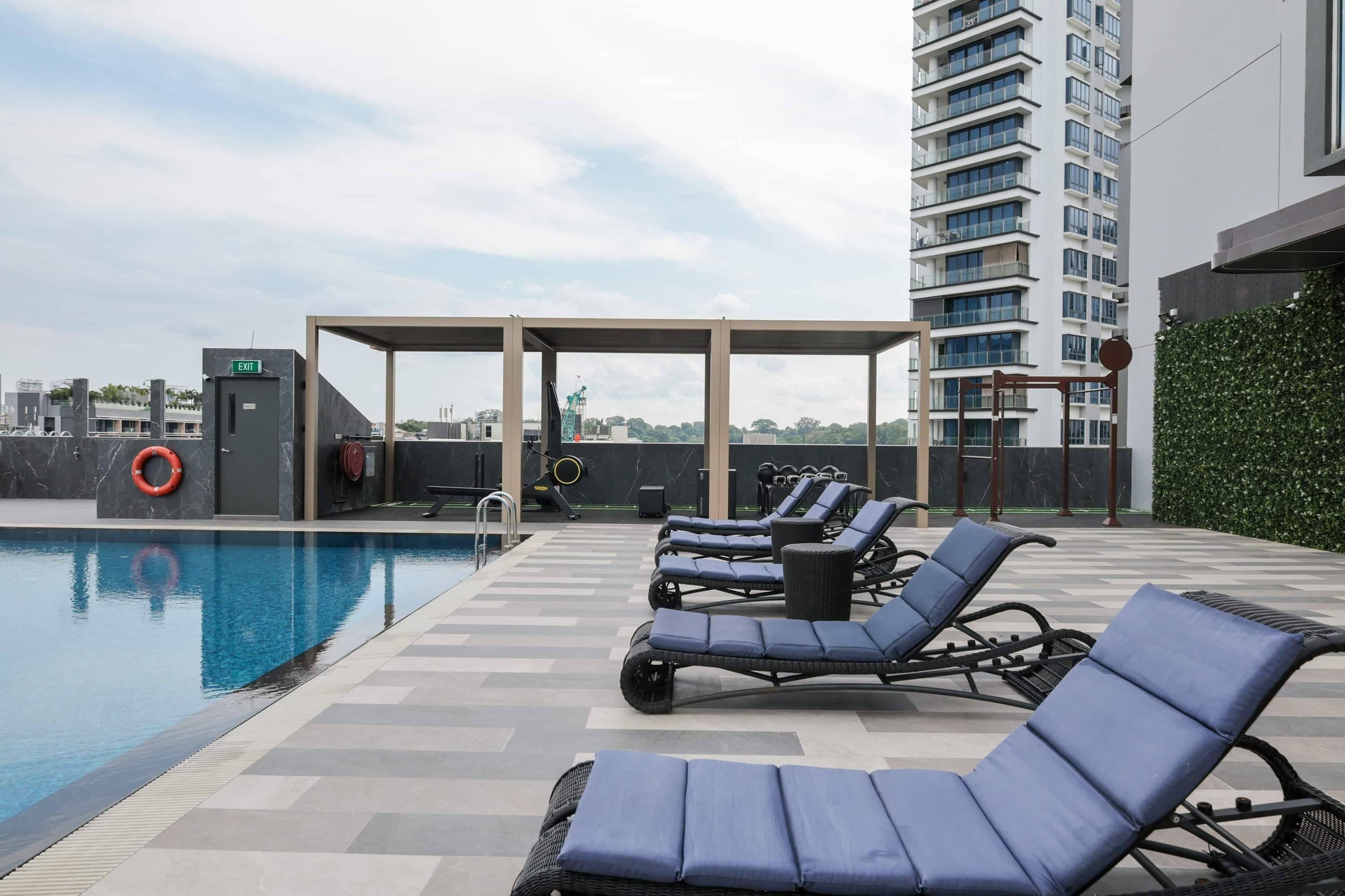Uma área de piscina no terraço, com espreguiçadeiras, um espaço de estar coberto e um prédio alto ao fundo.