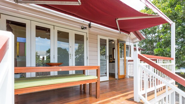 Um deck de madeira com um banco, um toldo vermelho e um corrimão branco.