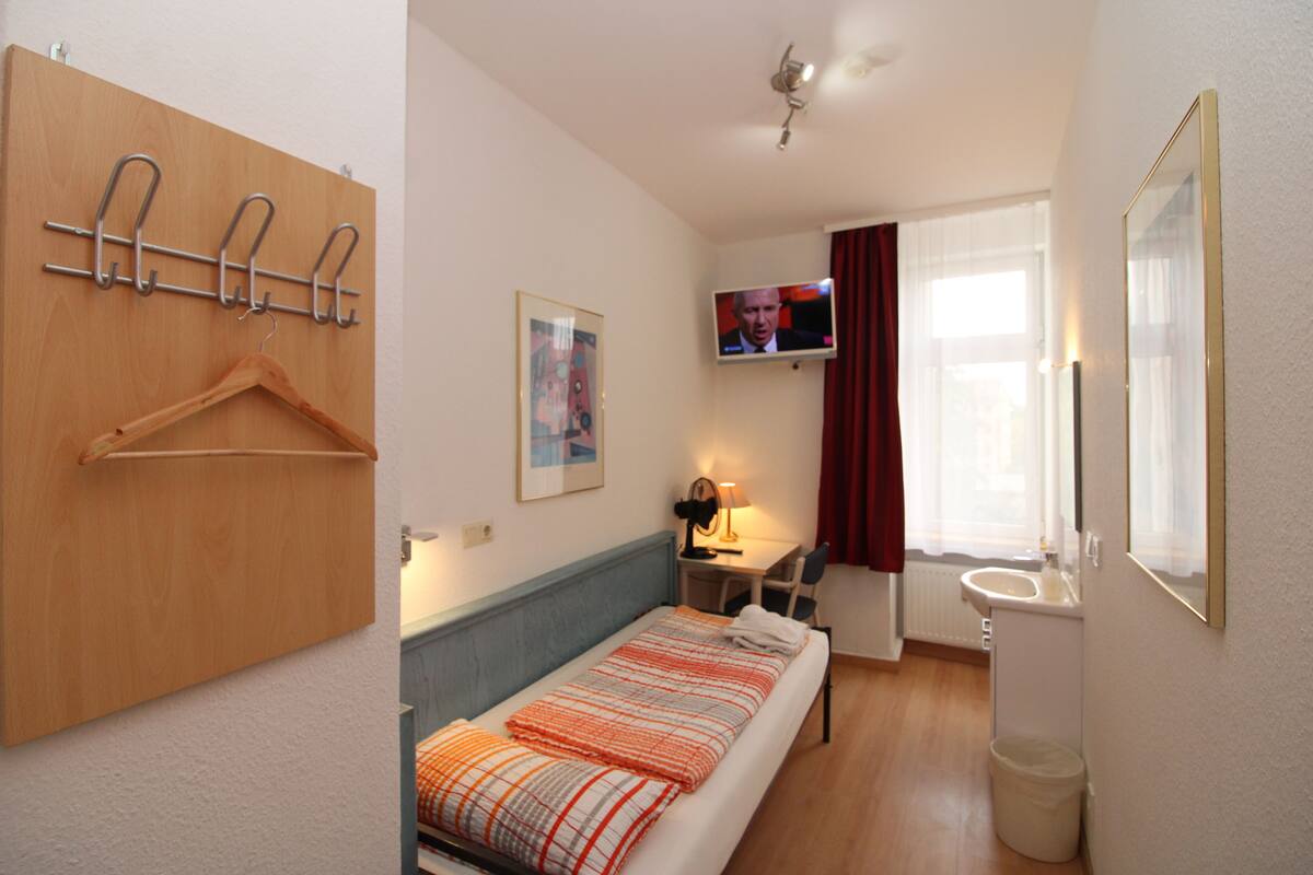 Quarto de hotel com cama, escrivaninha, cadeira, televisão, espelho e janela com cortinas.