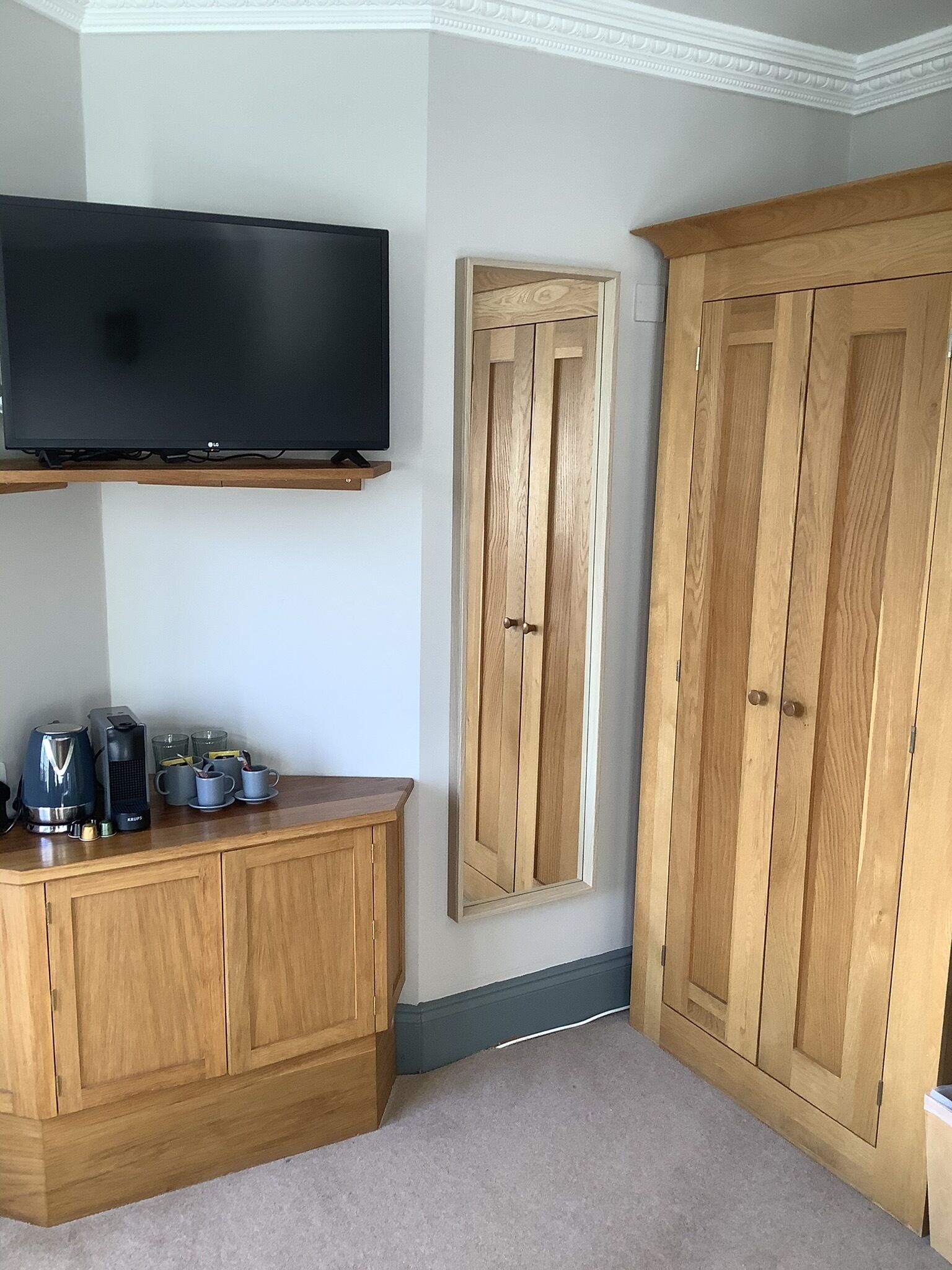 Quarto com televisão de tela plana fixada numa prateleira de madeira, guarda-roupa de madeira e porta de madeira.