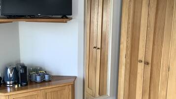 Quarto com televisão de tela plana fixada numa prateleira de madeira, guarda-roupa de madeira e porta de madeira.