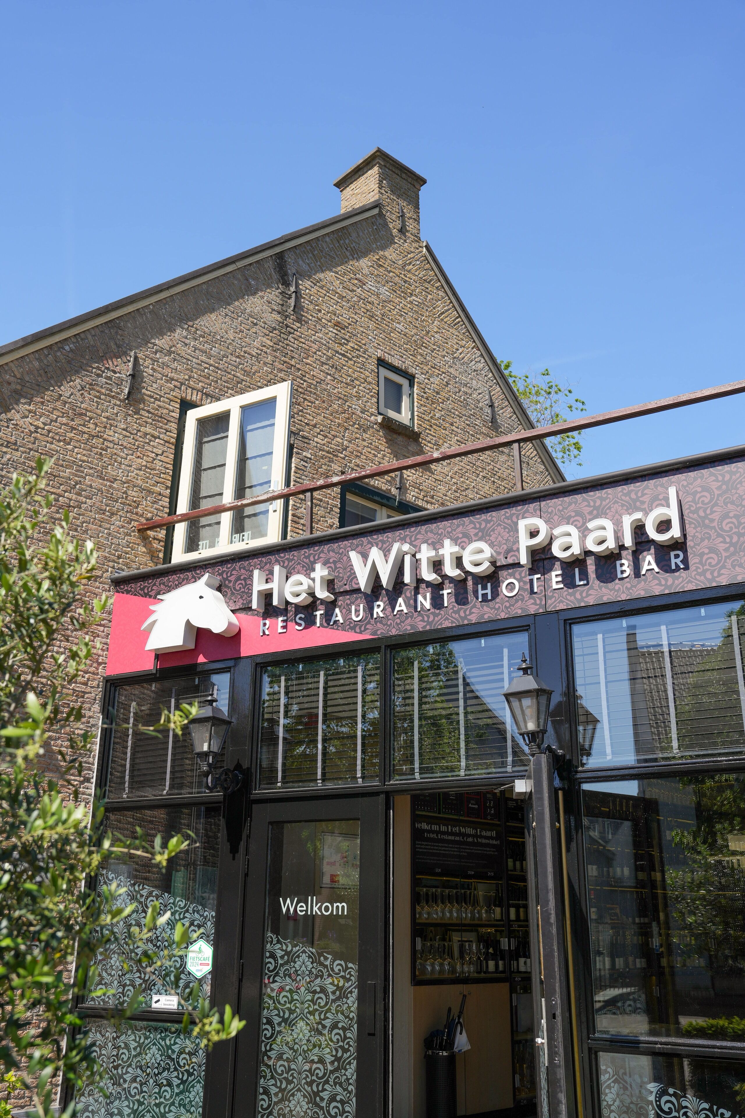 Exterior do restaurante e hotel Het Witte Paard, com fachada de tijolos e grandes janelas.