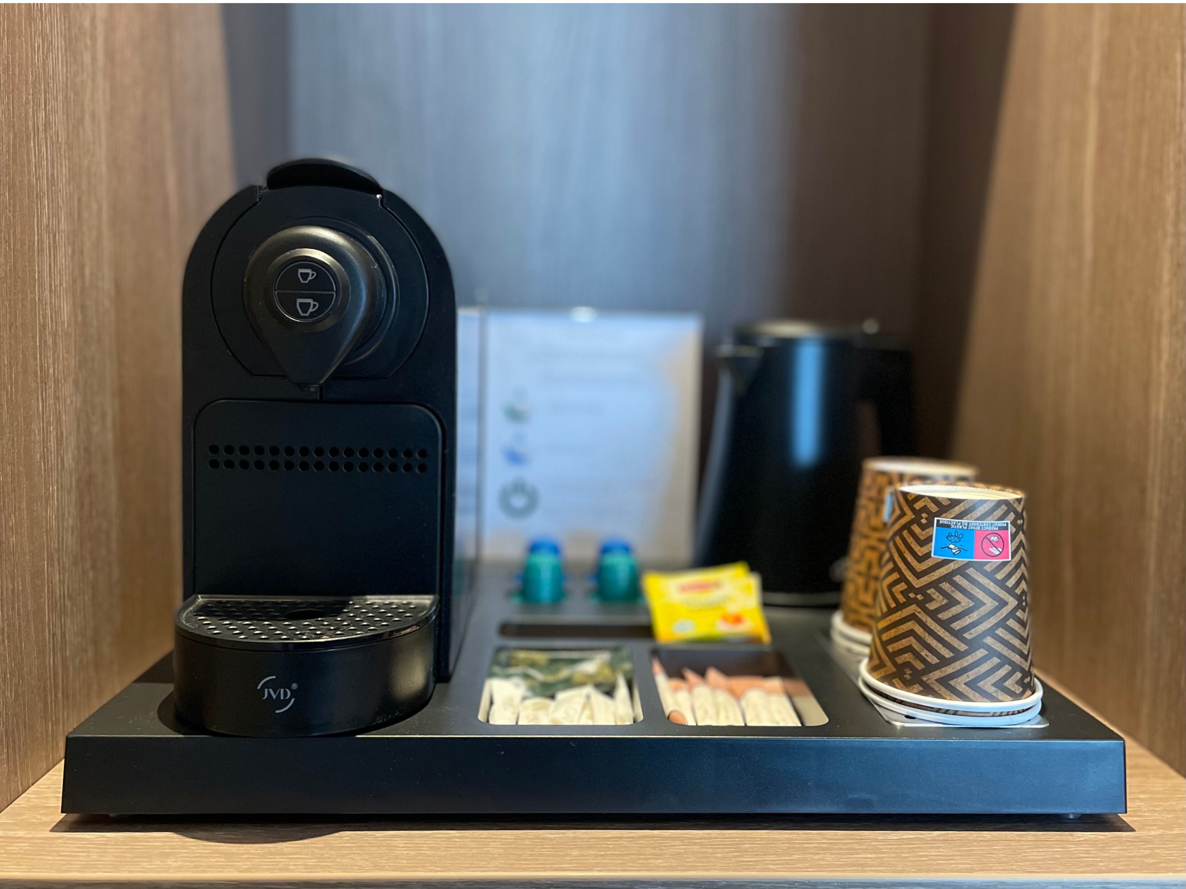 Máquina de café com suporte para xícara, chaleira e bandeja com lanches e uma xícara estampada.