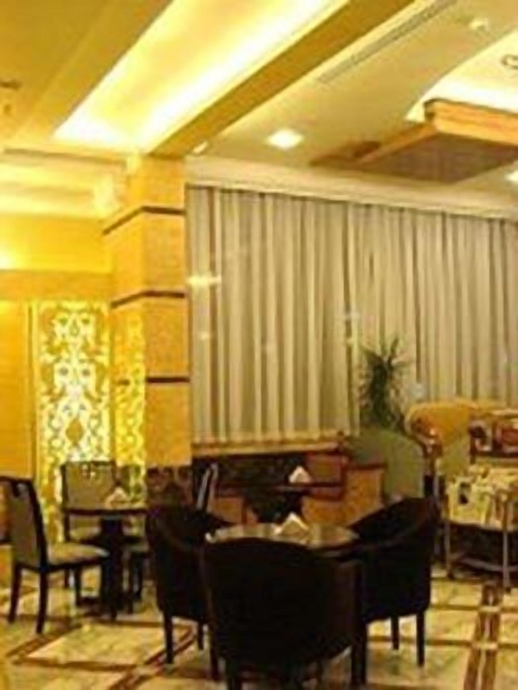 Um saguão de hotel com balcão de recepção, área de estar e uma grande janela com cortinas.