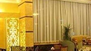 Um saguão de hotel com balcão de recepção, área de estar e uma grande janela com cortinas.