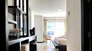 Quarto de hotel com uma cama, uma escrivaninha com computador, uma cadeira e uma janela com cortinas.