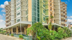 Um hotel com vários andares e design moderno, com varandas em cada andar, entrada coberta e vegetação exuberante na frente.