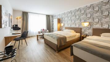 Quarto de hotel com duas camas, uma escrivaninha, uma cadeira e uma janela grande com cortinas.