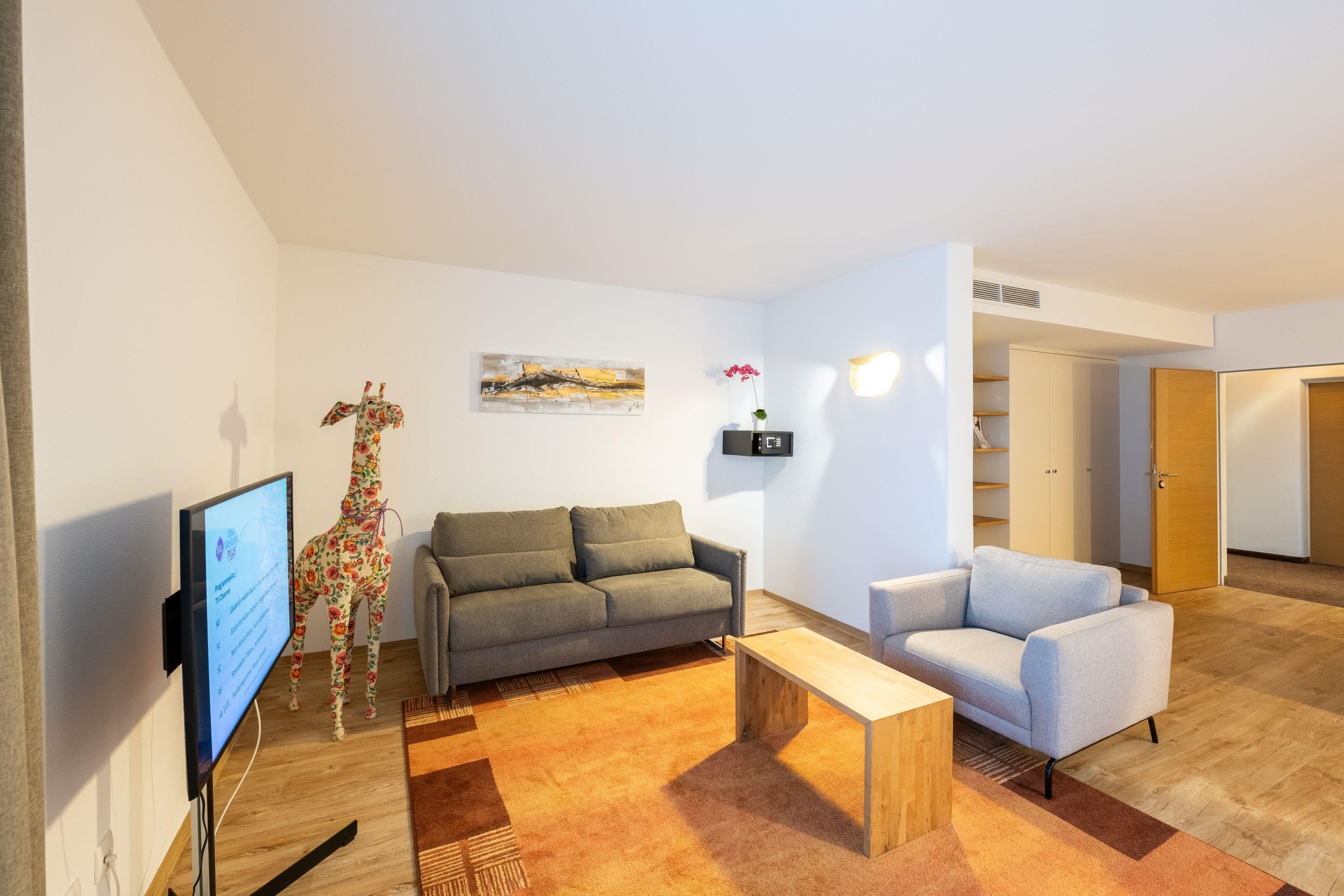 Uma sala de estar com sofá, mesa de centro, televisão e uma estátua de girafa.