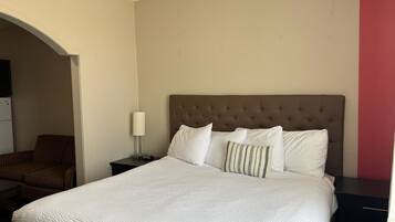 Quarto de hotel com uma cama grande, mesa de cabeceira com abajur, cadeira e televisão.