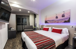 Quarto de hotel moderno com uma cama grande, um espaço de estar e uma pintura da paisagem urbana na parede.