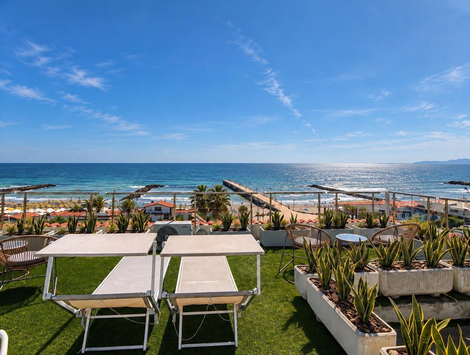 Terraço no telhado com espreguiçadeiras e vasos, com vista para uma praia e oceano.