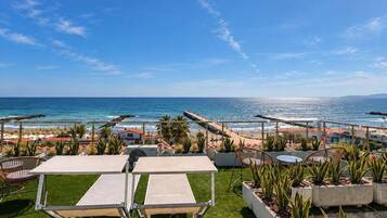 Terraço no telhado com espreguiçadeiras e vasos, com vista para uma praia e oceano.
