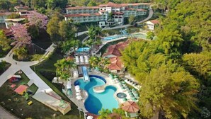 Resort com várias piscinas, um toboágua central e vegetação exuberante.