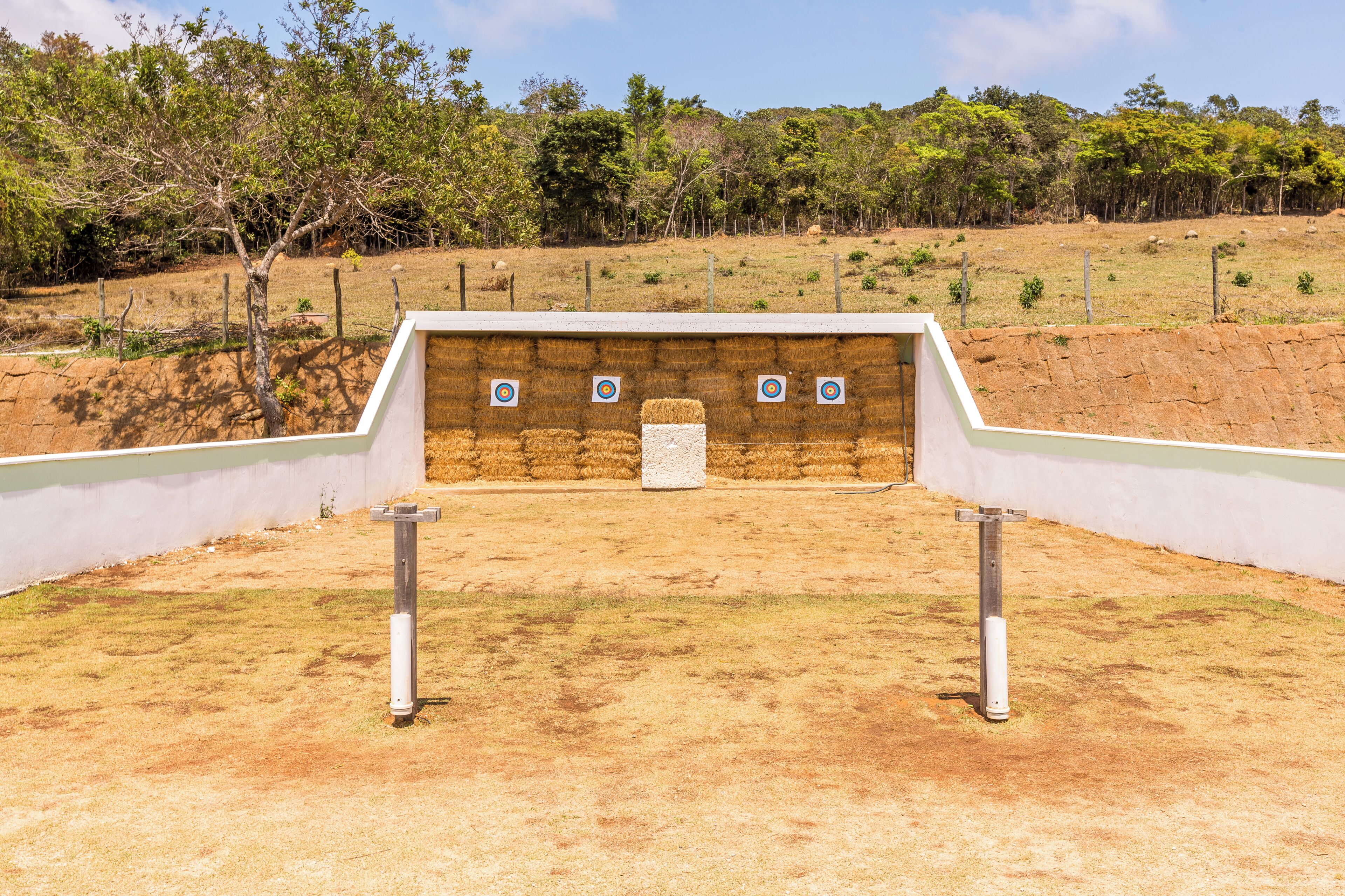 Um campo de tiro ao ar livre com quatro alvos, cercado por uma área vedada e um gramado.