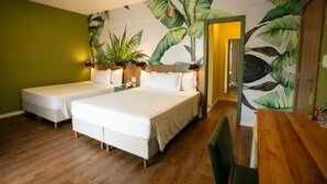 Quarto de hotel com duas camas, uma mesa de jantar de madeira e parede verde com um mural de folhas tropicais.