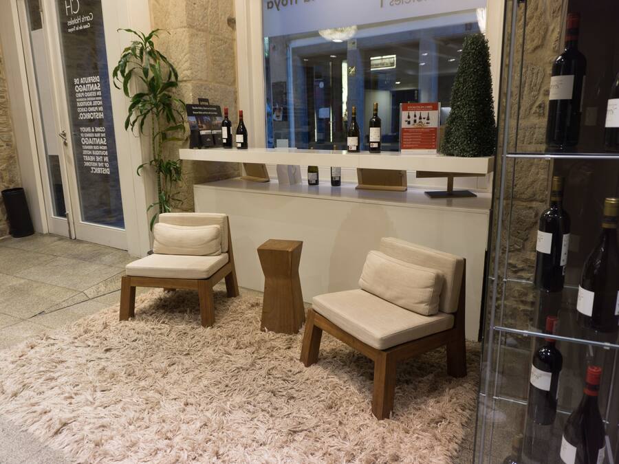 Um hall de hotel com duas cadeiras de madeira, um tapete fofo, uma vitrine de vidro com garrafas de vinho e uma parede de pedra.