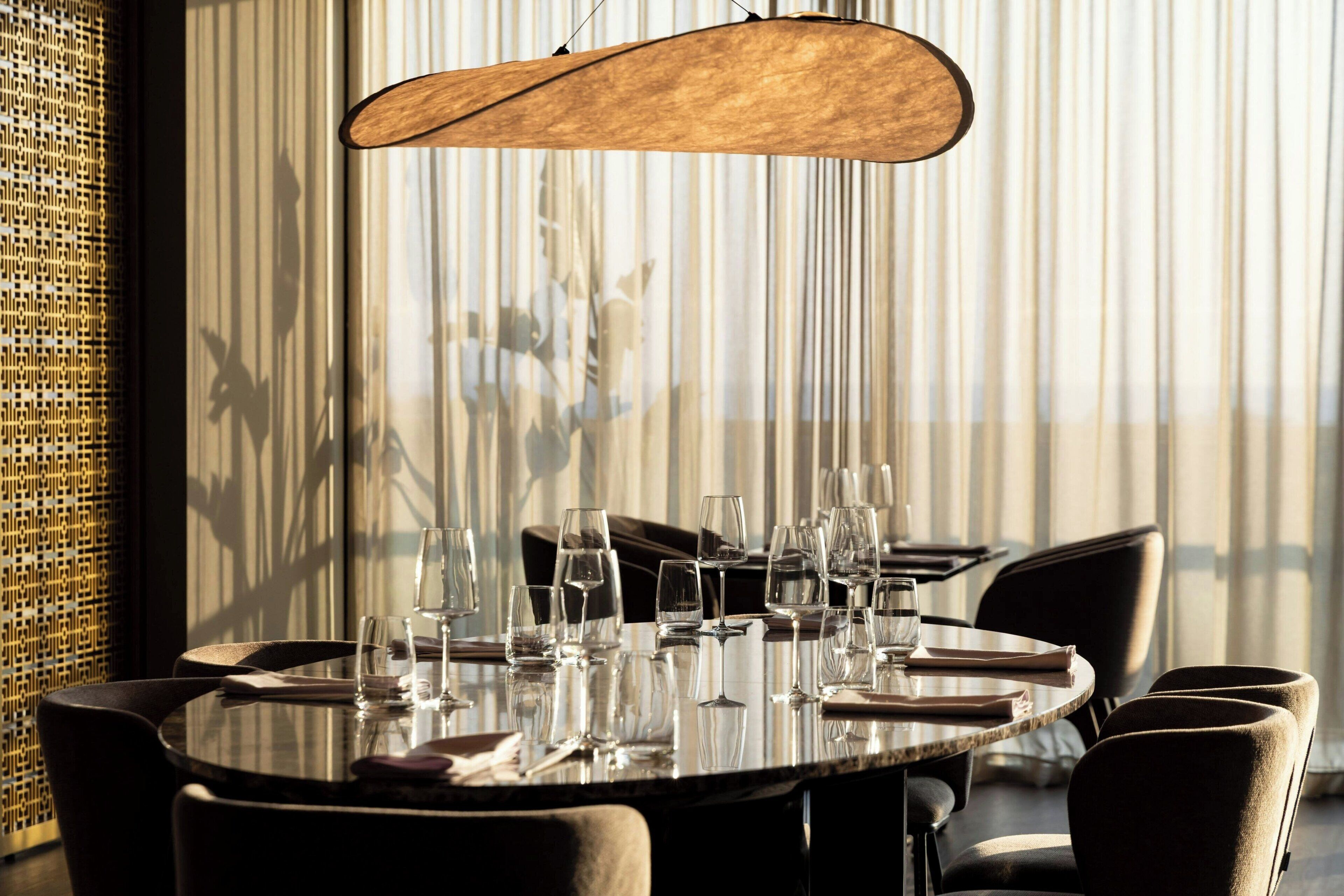 Uma sala de jantar com uma mesa redonda posta para refeição, cercada por cadeiras, e um lustre pendurado acima.