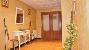 Um corredor com um console branco, um espelho, uma porta com persianas e uma planta em vaso.