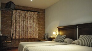Quarto de hotel com duas camas, uma parede de tijolos, uma televisão e uma mesa de cabeceira com abajur.