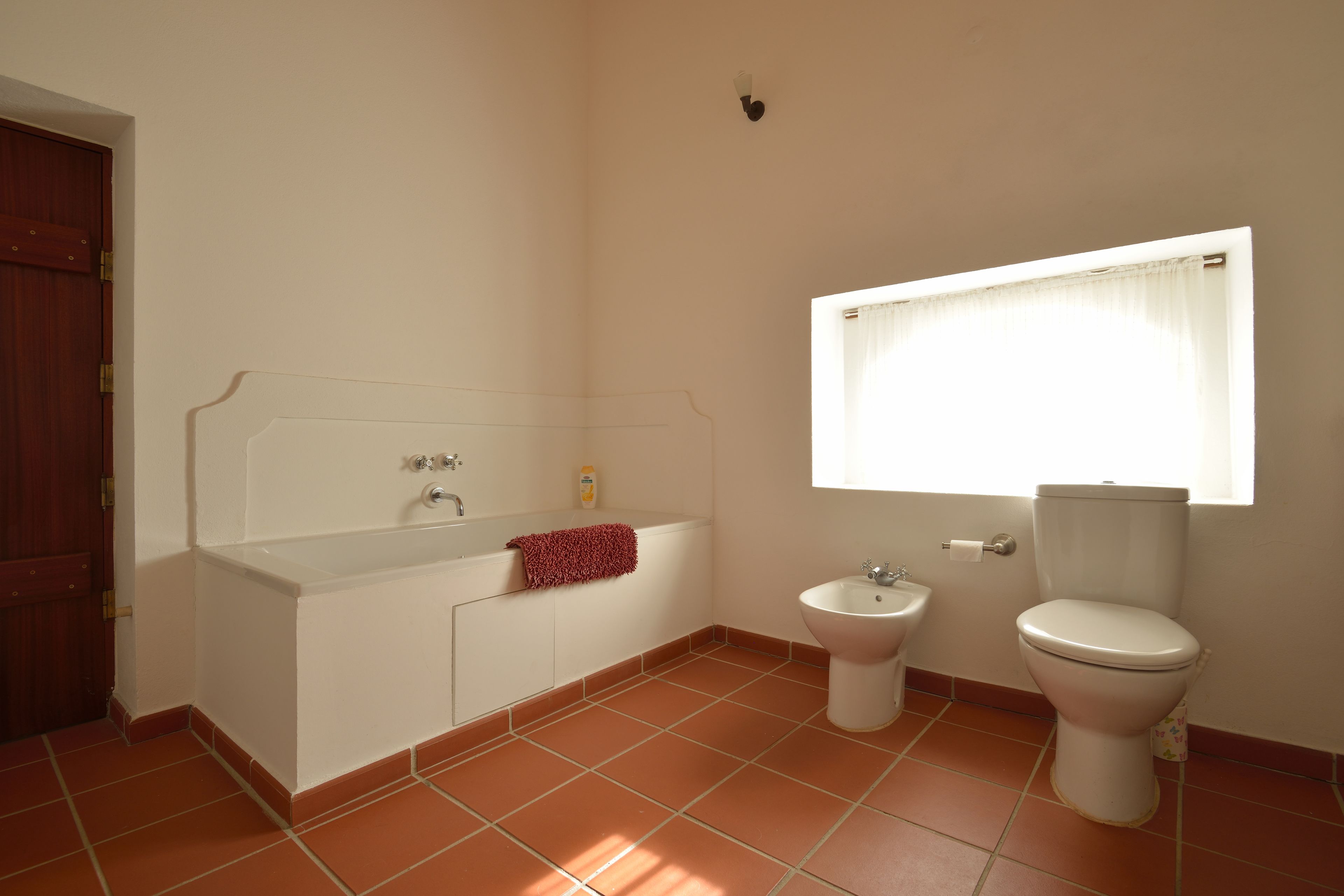 Casa de banho com banheira, lavatório e sanita, com uma janela e cortinas.