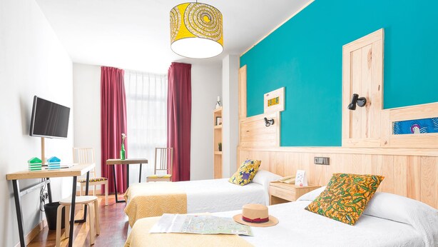 Quarto de hotel com duas camas, uma escrivaninha, uma cadeira, uma televisão e uma janela com cortinas.