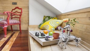 Um quarto aconchegante com piso de madeira, uma cadeira vermelha, um banco de madeira e uma bandeja com lanches e um vaso com uma rosa.