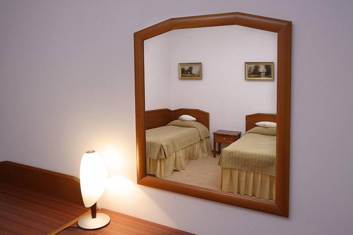 Quarto com duas camas de solteiro, mesa de cabeceira, criado-mudo e espelho com moldura de madeira.
