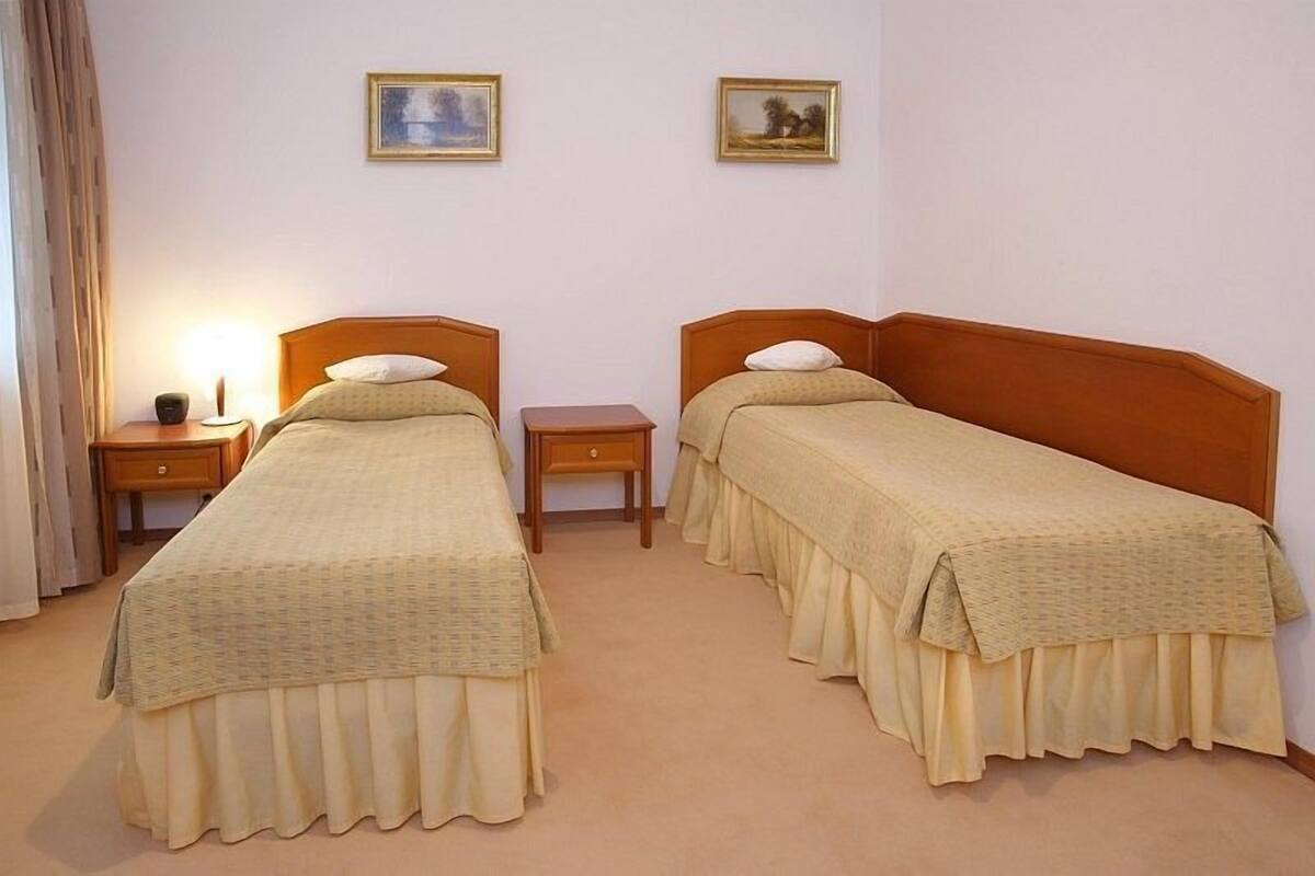 Quarto com duas camas de solteiro, cada uma com cabeceira de madeira e mesa de cabeceira. Duas imagens emolduradas estão penduradas na parede acima das camas.