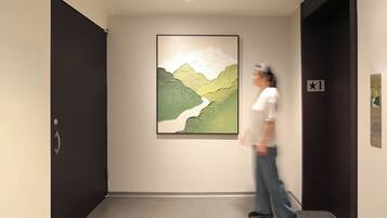 Um corredor com um quadro de uma paisagem montanhosa, uma porta e uma placa indicando o número do quarto 1.