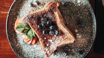 Um prato com sanduíche tostado, amoras e uma folha de hortelã.