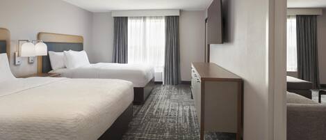Quarto de hotel com duas camas, uma escrivaninha, televisão de tela plana e uma grande janela com cortinas.