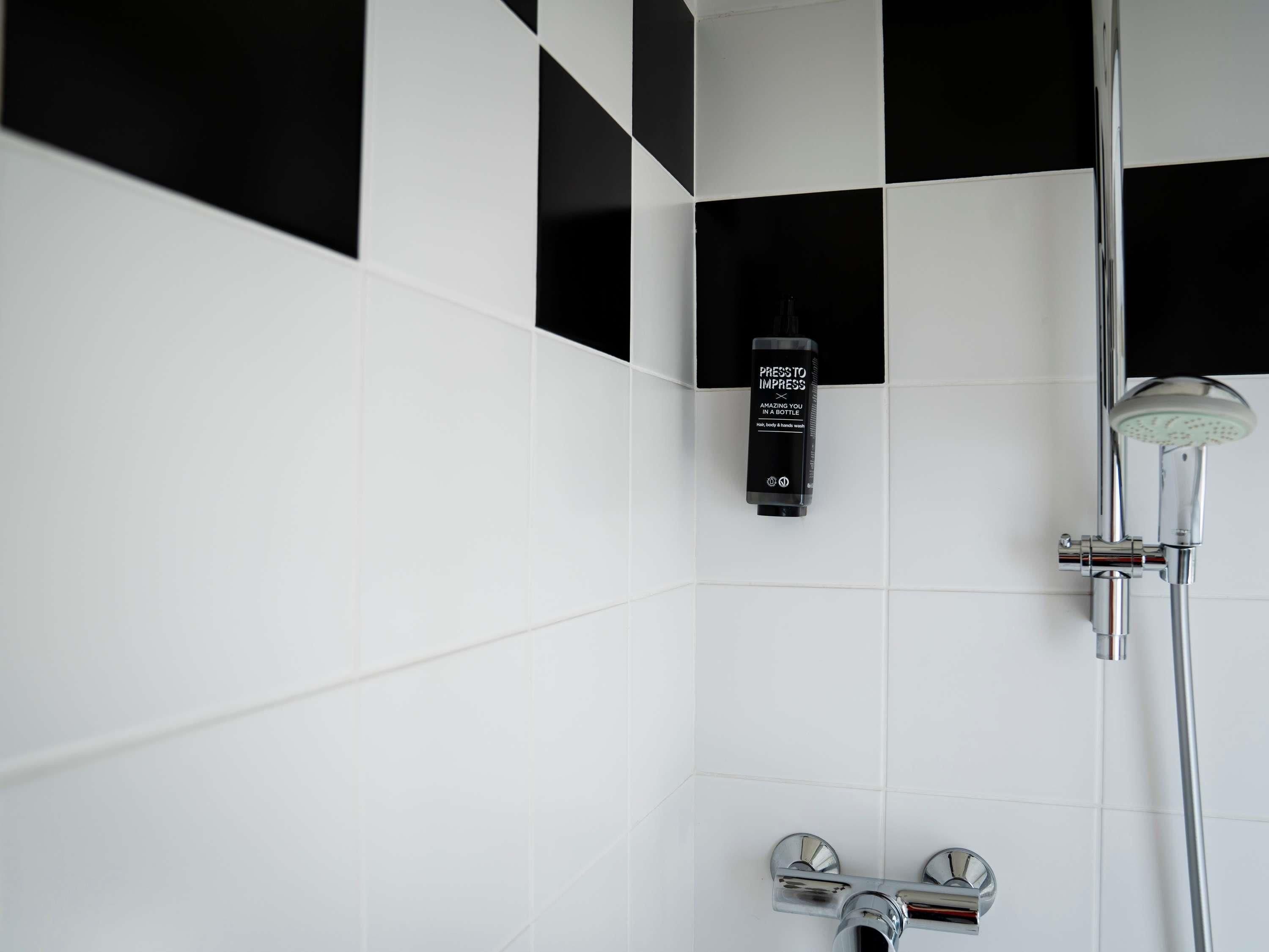 Casa de banho moderna com parede quadriculada em preto e branco, chuveiro manual e frasco de loção corporal.