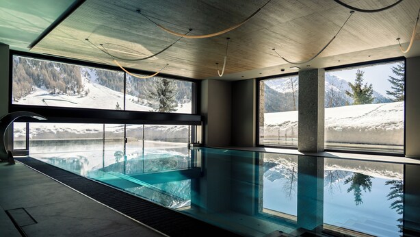 Piscina interna com amplas janelas que oferecem vista para uma paisagem montanhosa coberta de neve.