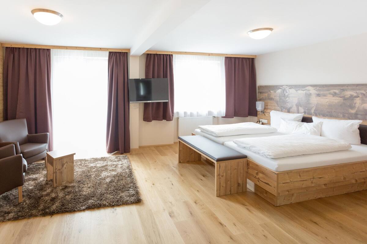 Quarto com cama de madeira, um banco, televisão e sofá.